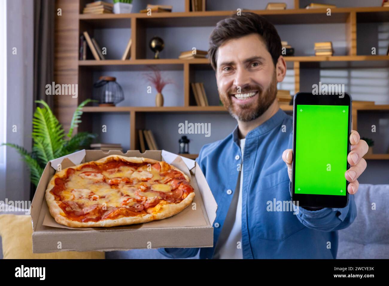 Cheerful adult male presents a mobile phone with a green screen next to ...