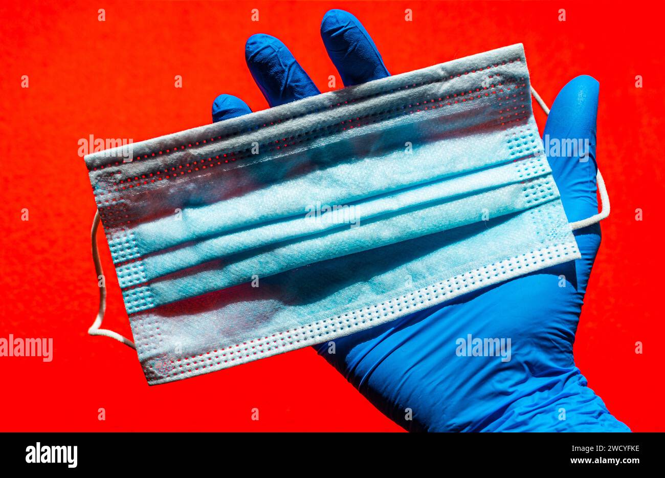 Disposable surgical mask in the doctor's hand on a red background ...