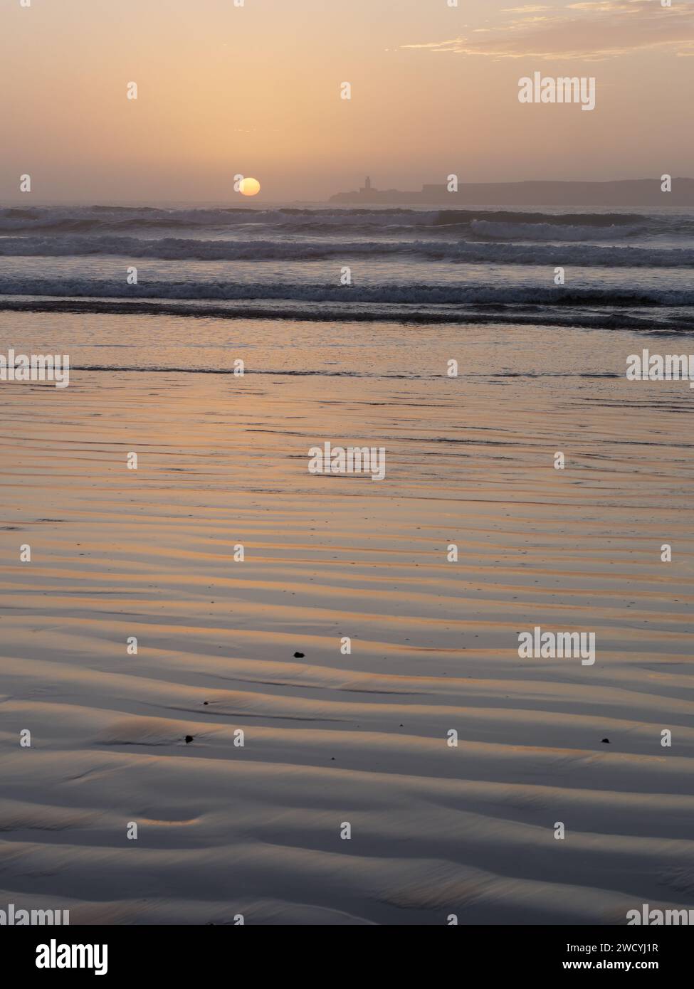 Sun sets next to an Island as light reflects in the water, in Essaouira ...