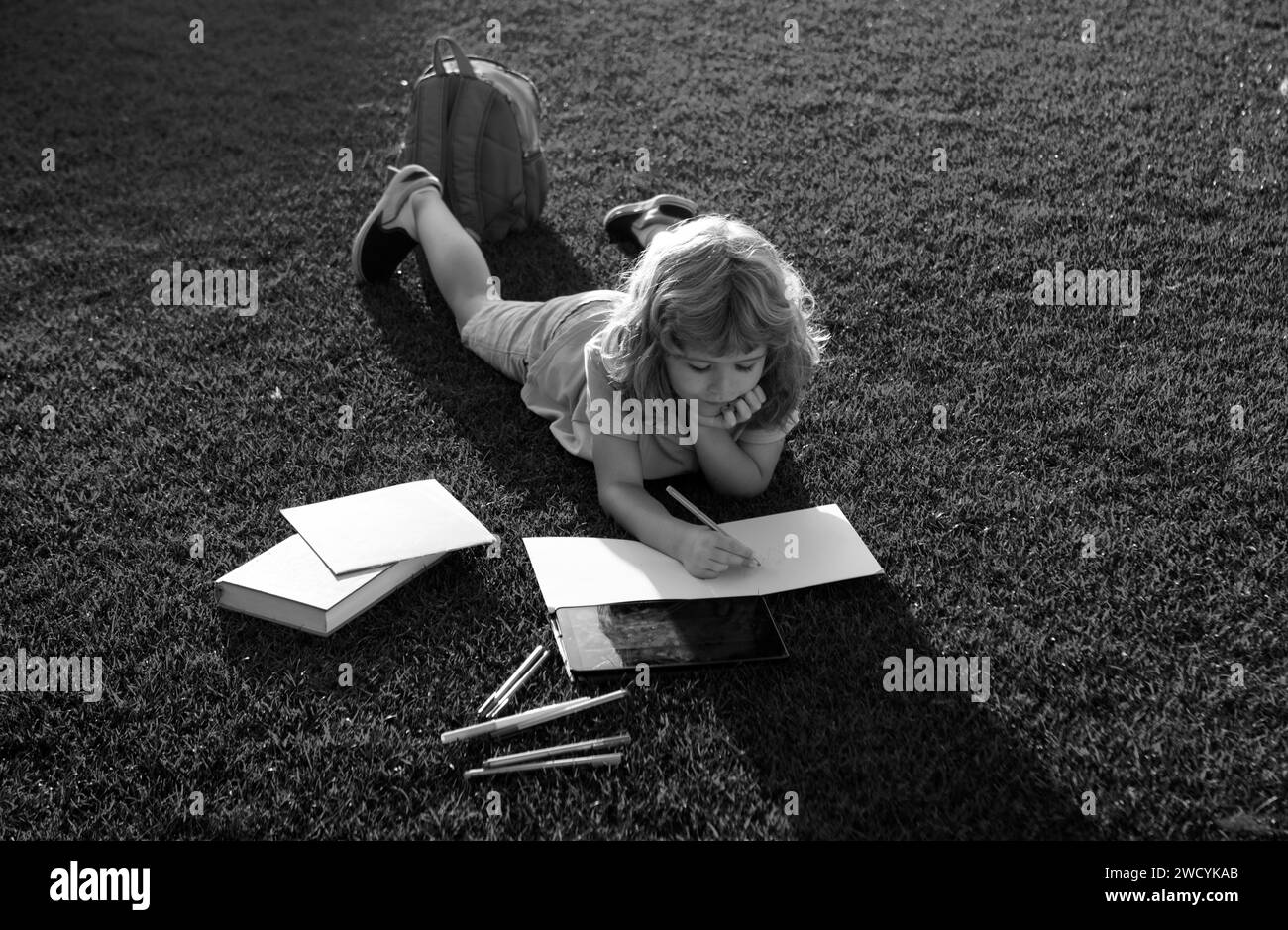Cute boy reading book on green grass writing notes in copybook ...