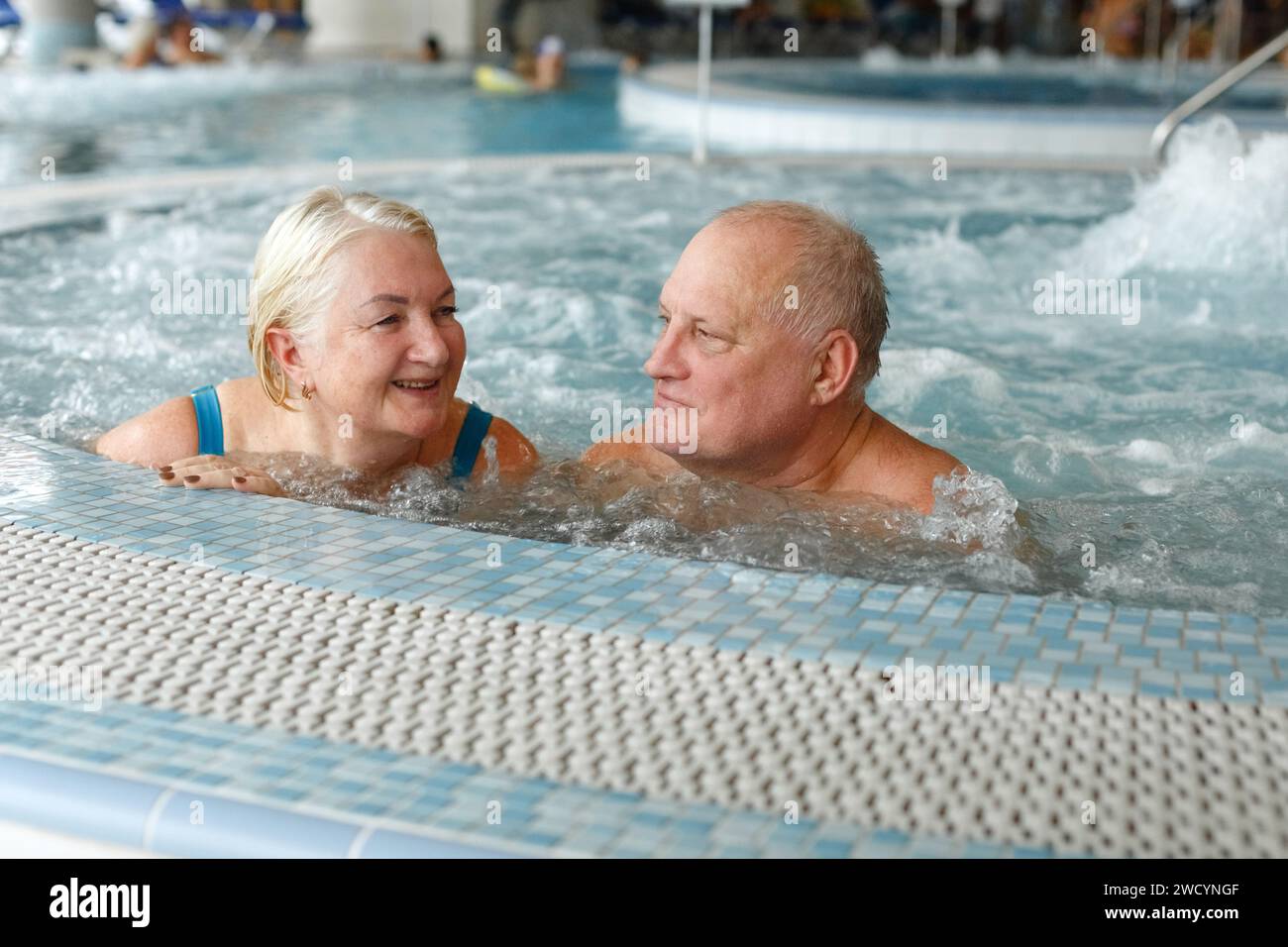 Happy elderly couple enjoying hydromassage in the swimming pool at the ...