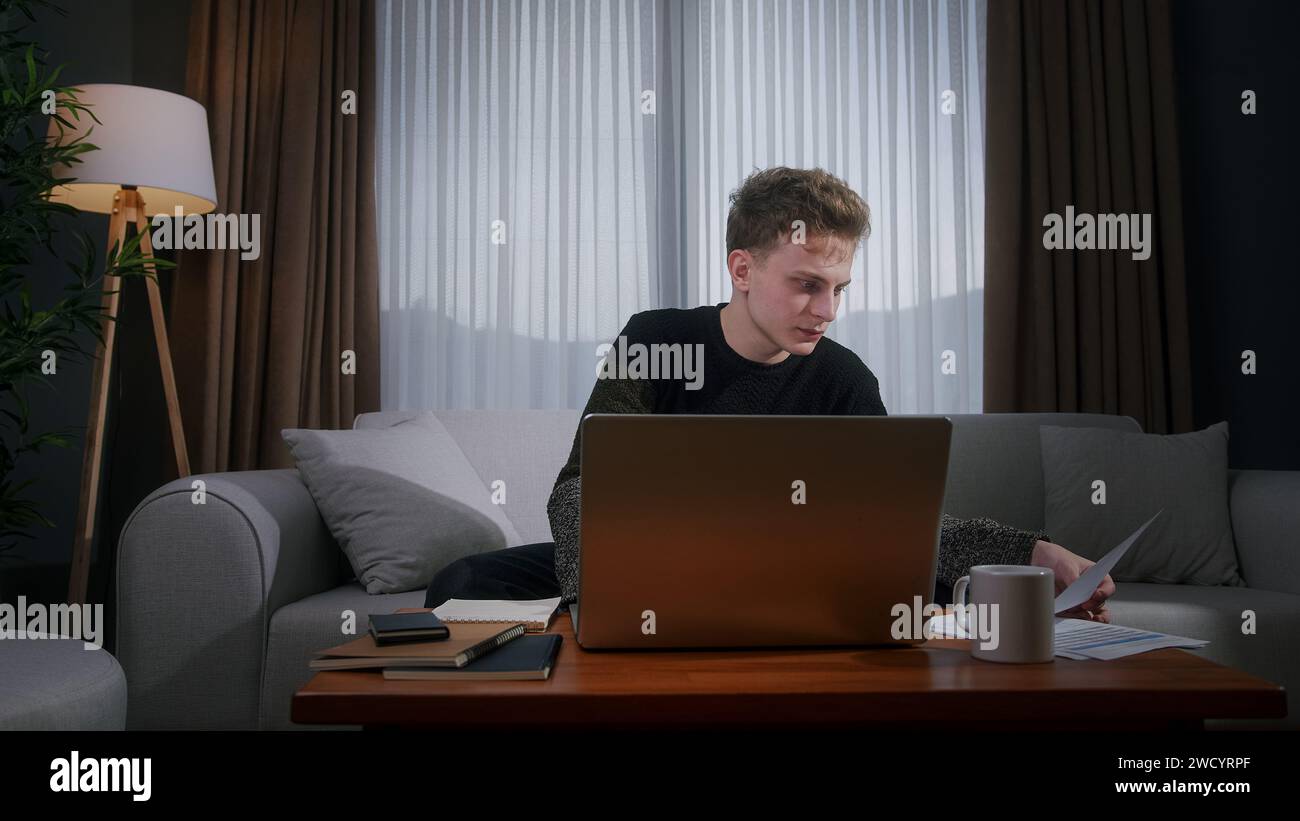 Focused blonde man working from home using with laptop while sitting on ...