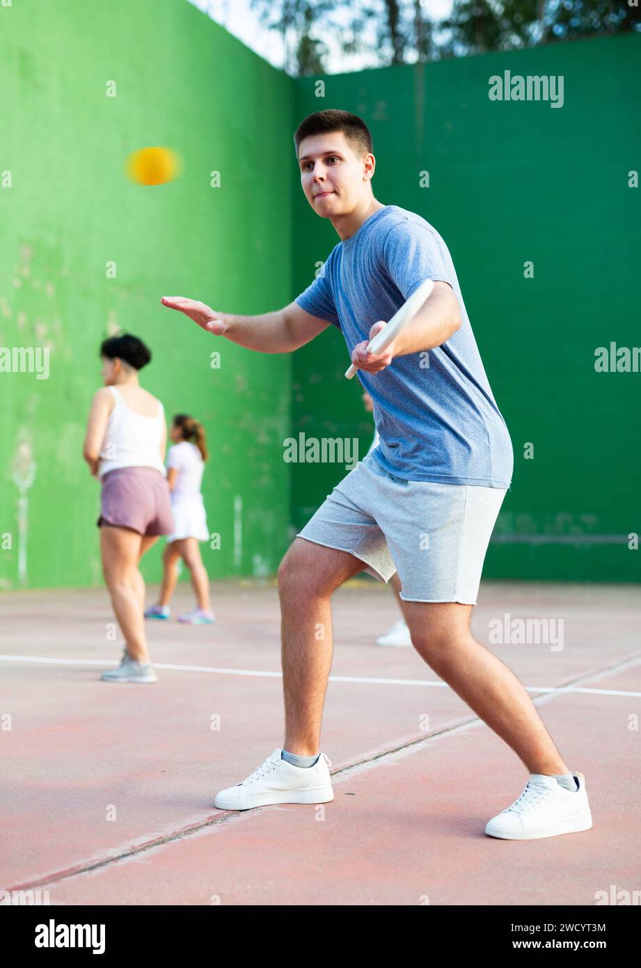 Concentrated young man paleta fronton player hitting ball with racket ...