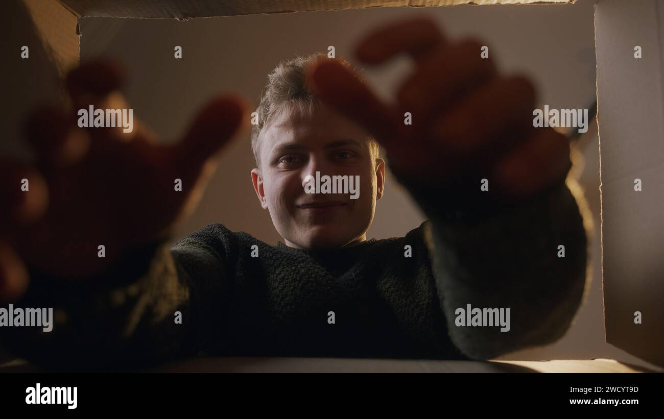 Close-up inside of carton box bottom view, young blonde man opens ...