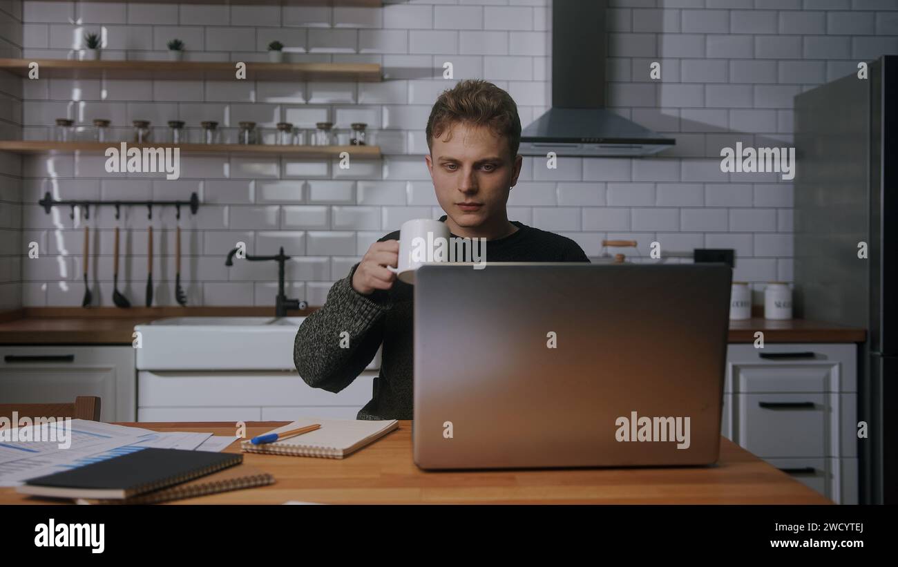 Young university student sitting in the kitchen at home, looking laptop ...