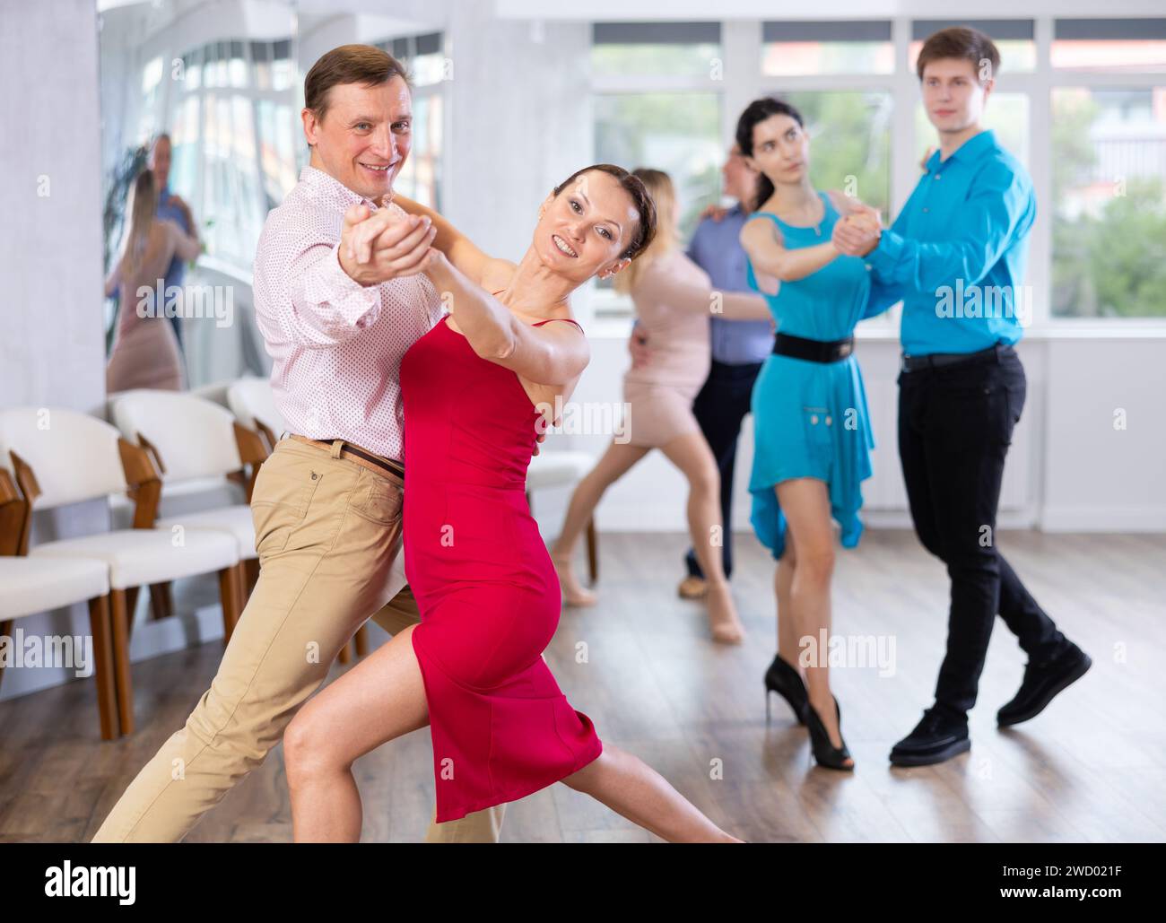 Happy people of different ages dancing tango in pairs in dance hall ...