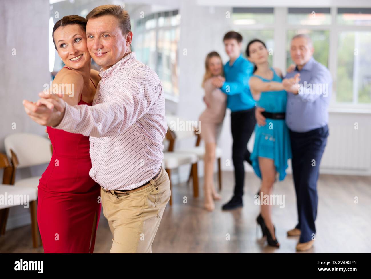 Happy people of different ages dancing tango in pairs in dance hall ...
