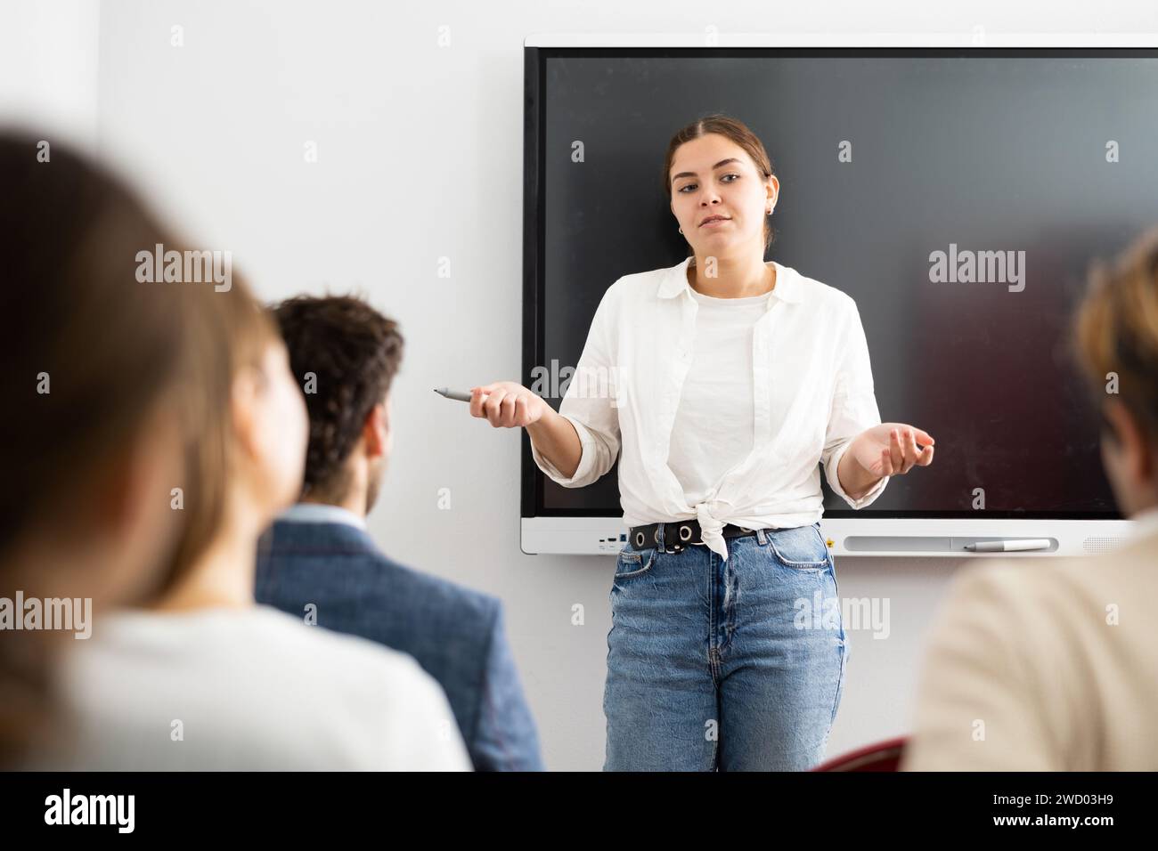 Young female professor explaining subject to classroom full of students ...