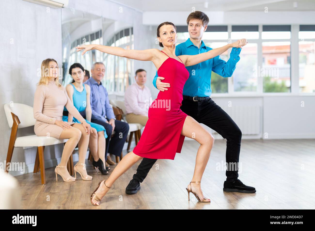 Brunette in red and young man enjoying tango in dance studio Stock ...