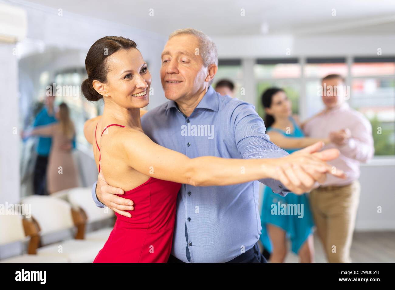 Happy people of different ages dancing tango in pairs in dance hall ...