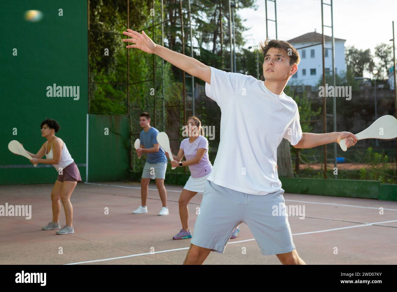 Sporty guy playing pelota with wooden racket on open fronton court ...