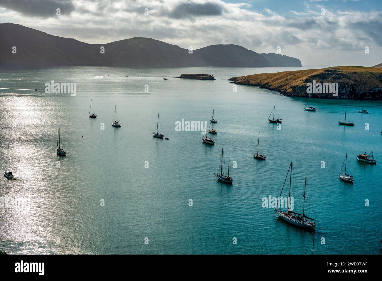Sail boats sailing and moored in the still ocean between the coastline ...