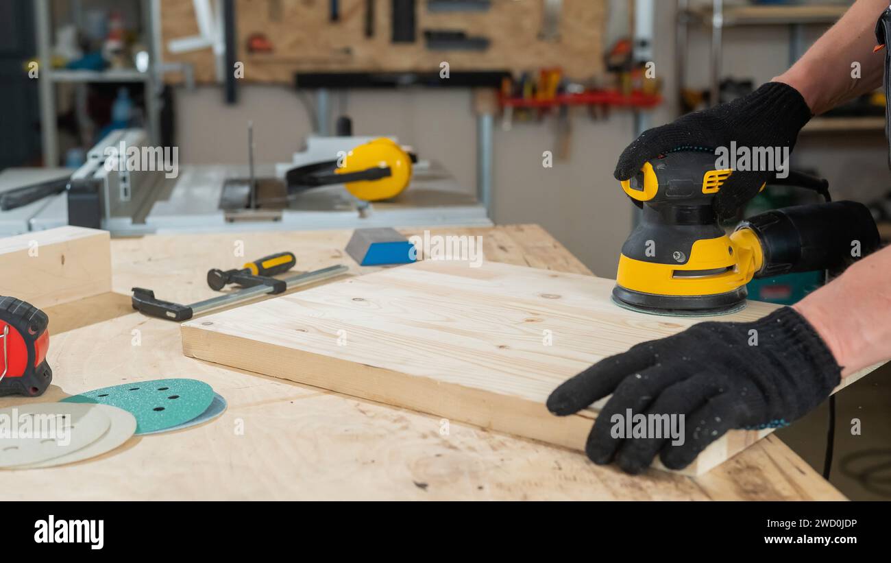 A man using an orbital wood sander in a workshop. Close-up of a ...