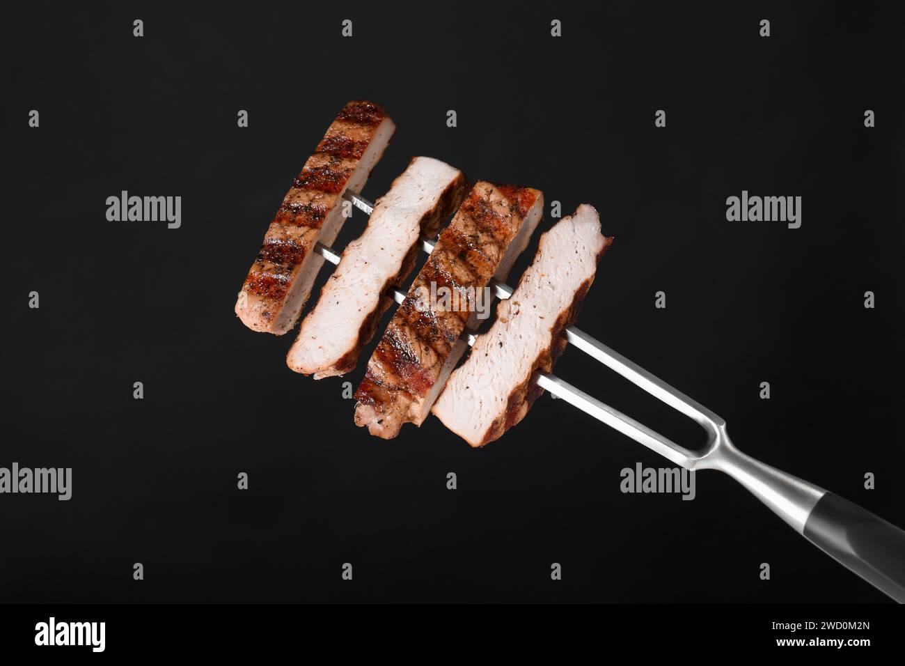 Carving fork with cut grilled pork steak pieces against black ...