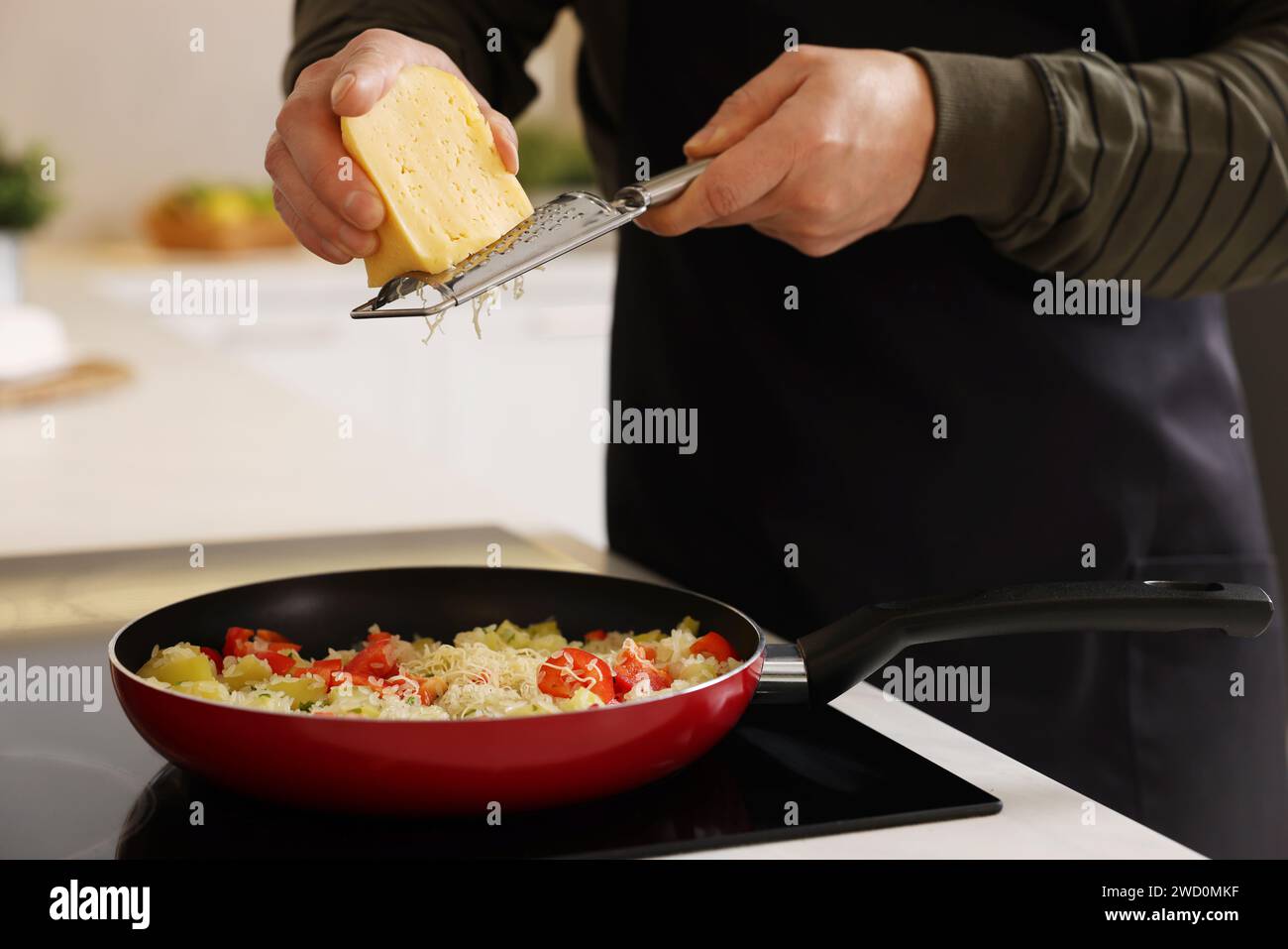 Cooking process. Man grating cheese into frying pan in kitchen, closeup ...
