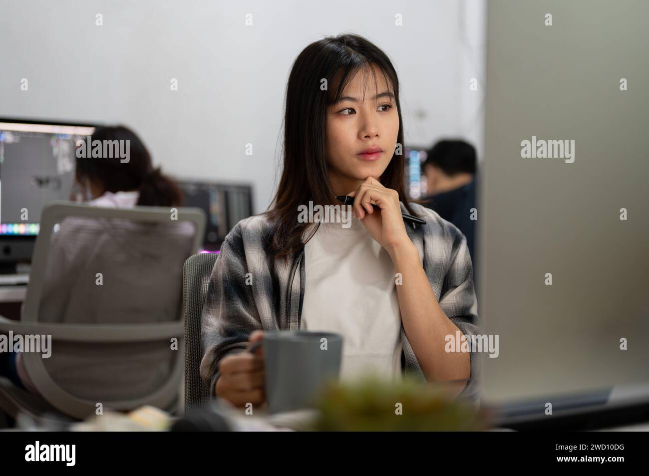 Concentrated young Asian female graphic designer is sipping coffee ...