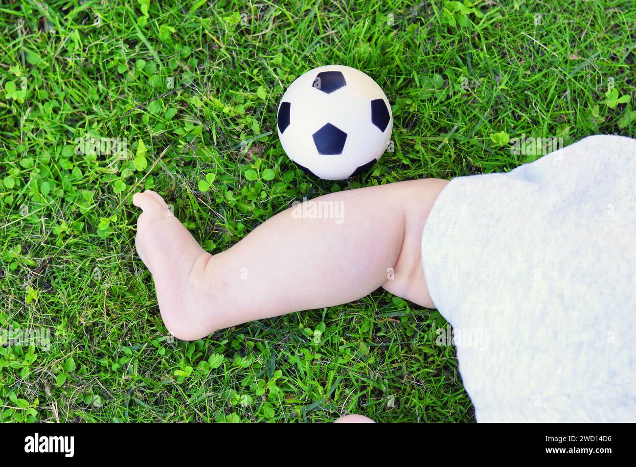 newborn kid laying on the grass with a small soccer ball. Sports and ...