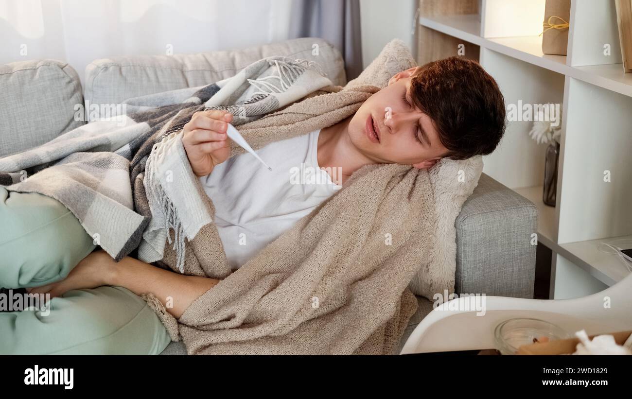 Cold fever temperature man thermometer couch home Stock Photo - Alamy