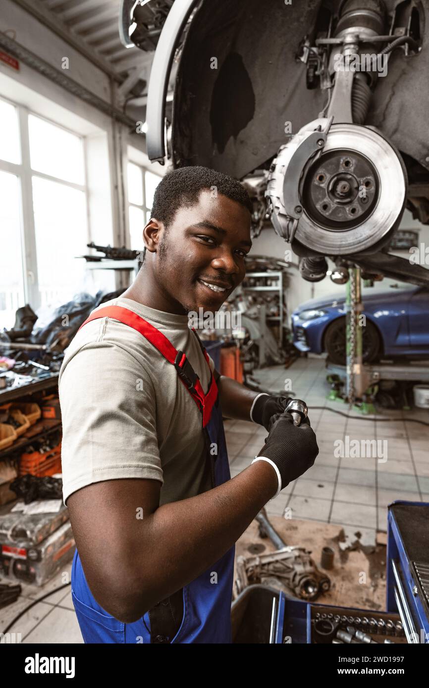 African male auto-mechanic repairing car brakes under the car in auto ...