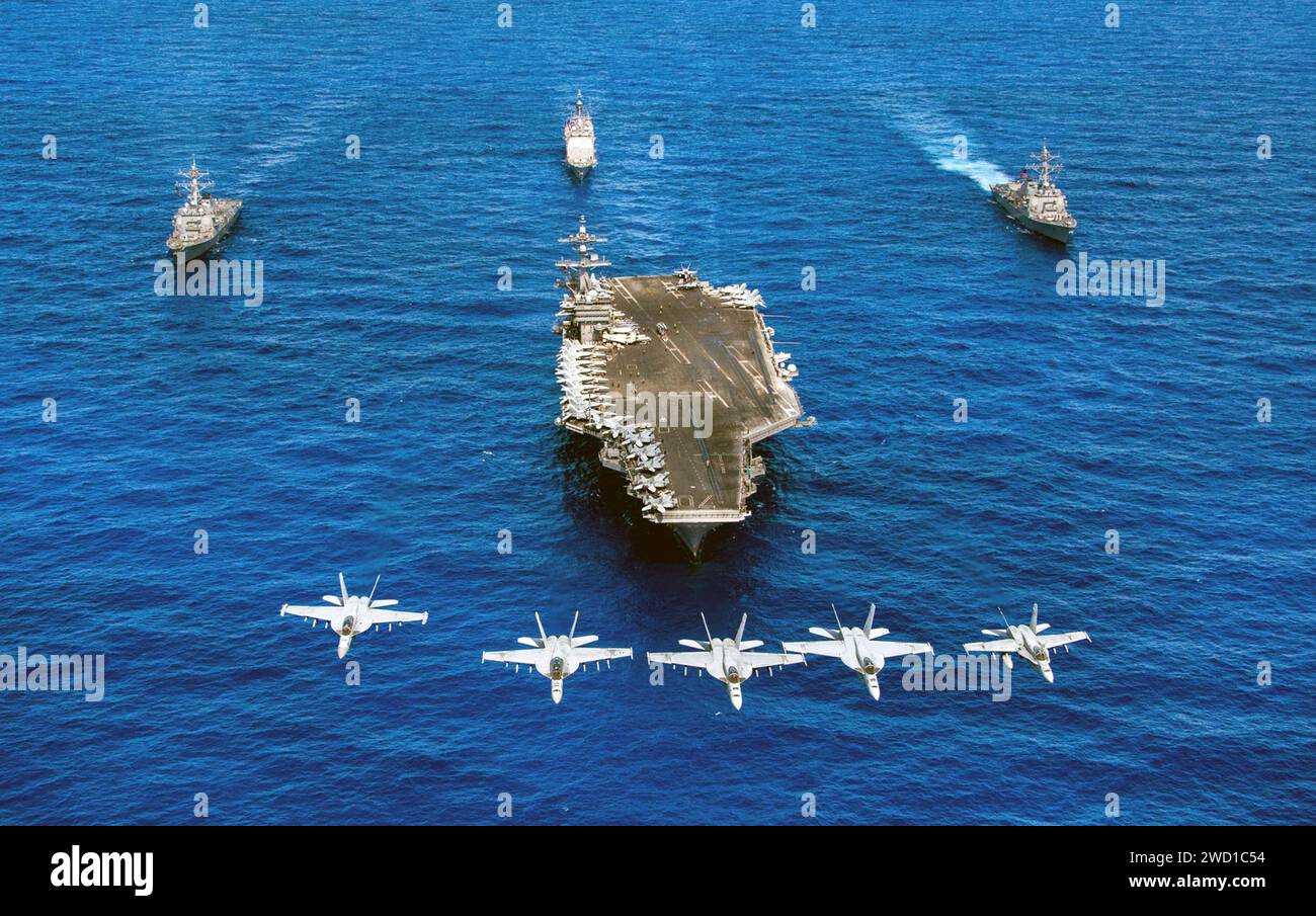 F/A-18 Hornets fly over a formation of U.S. Navy ships transiting the ...