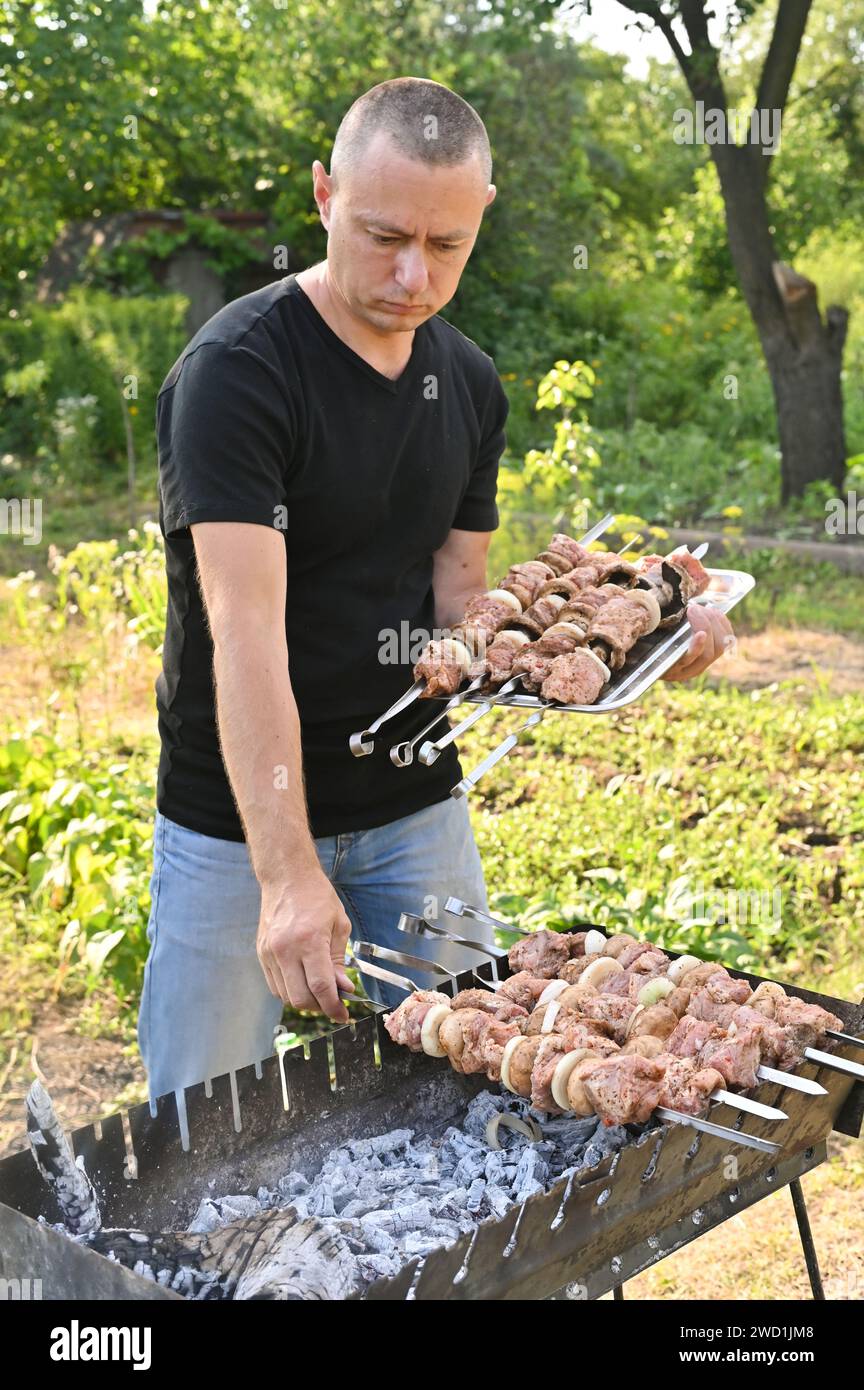 A man puts skewers with meat on the grill Stock Photo - Alamy