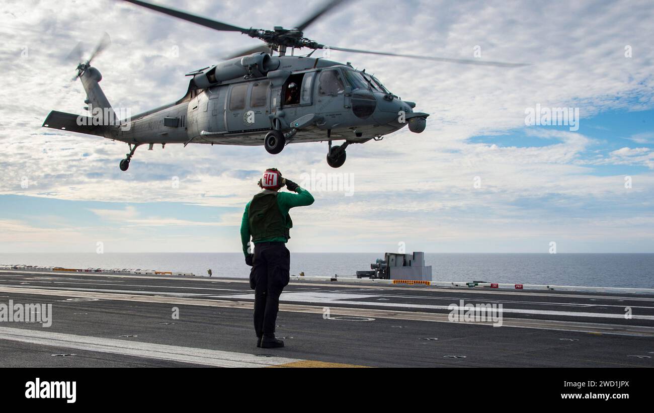 A Sailor salutes the crew of an MH-60S Sea Hawk as it takes off from ...