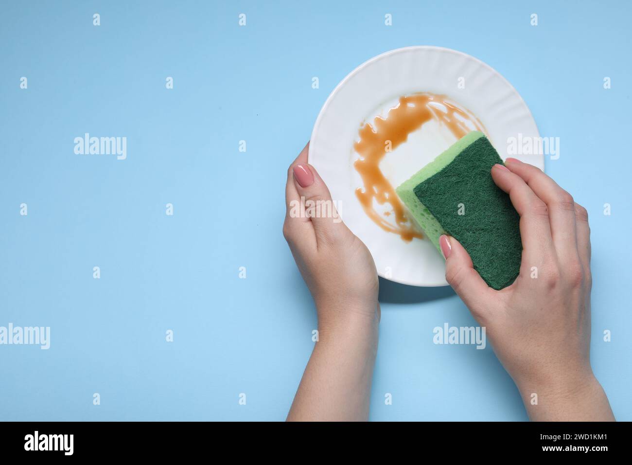 Woman washing dirty plate with sponge on light blue background, top ...