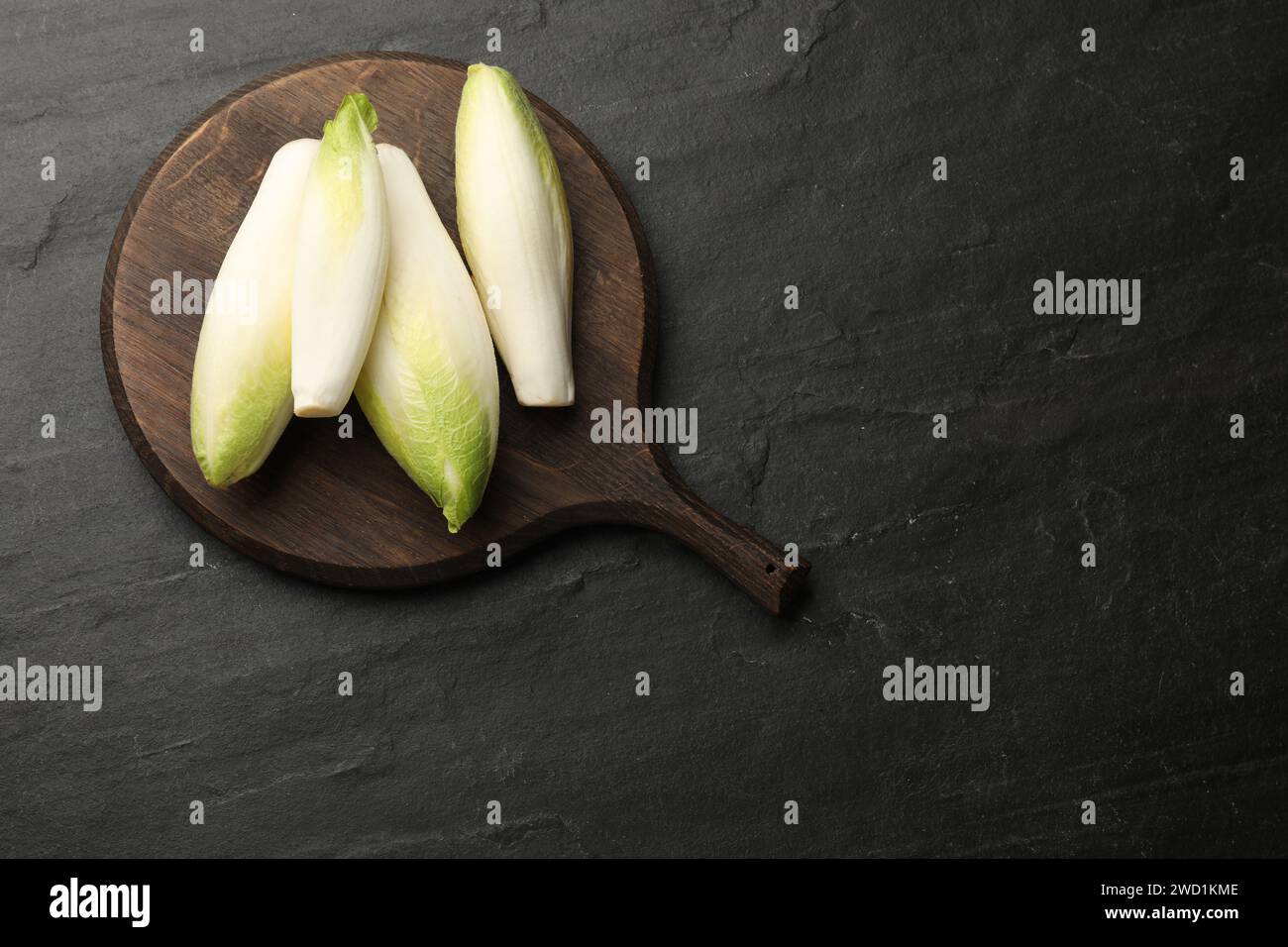 Fresh raw Belgian endives (chicory) on black table, top view. Space for ...