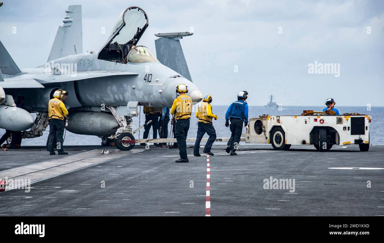 Sailors move an F/A-18C Hornet across the flight deck aboard the ...