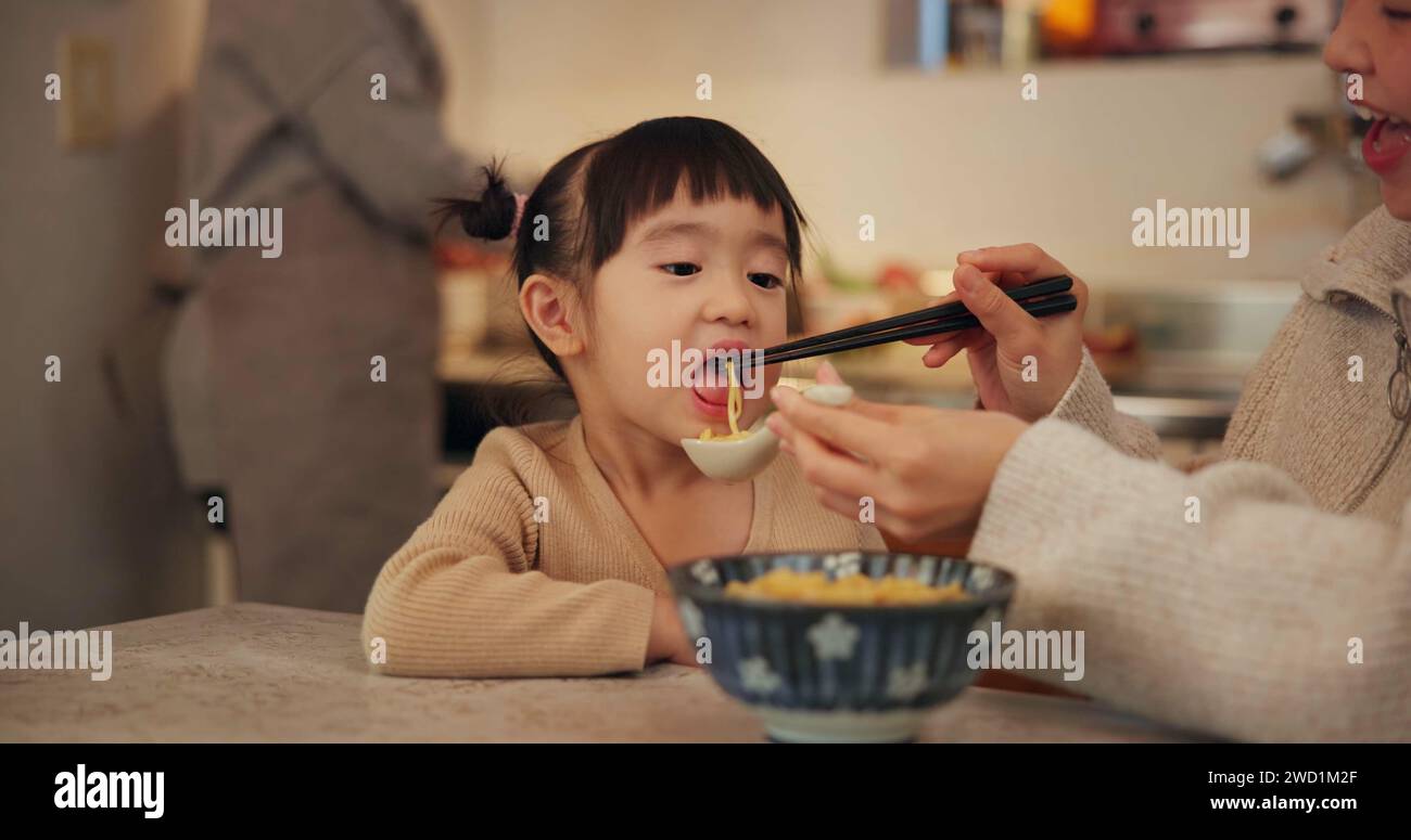 Family, Japanese and woman feeding daughter in kitchen of home for ...