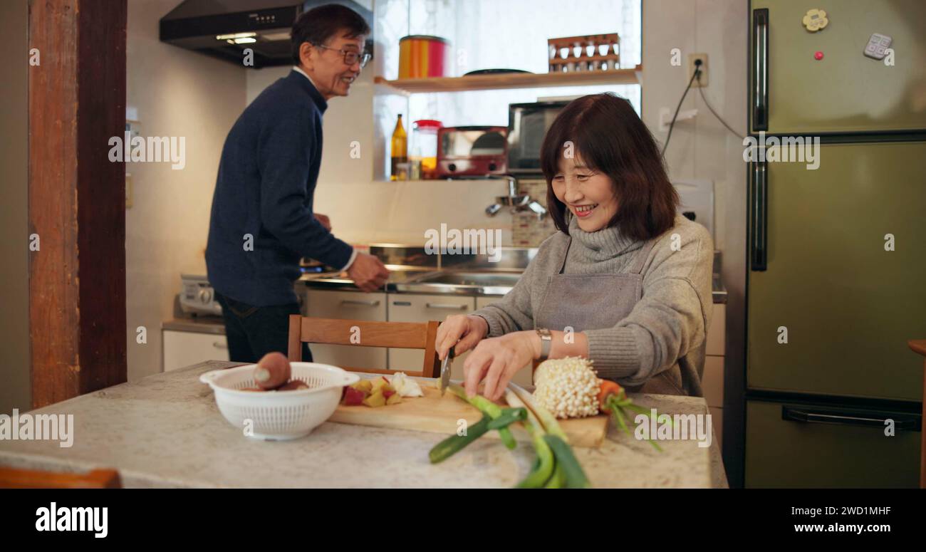 Cooking, conversation and Japanese couple in kitchen cutting vegetables ...