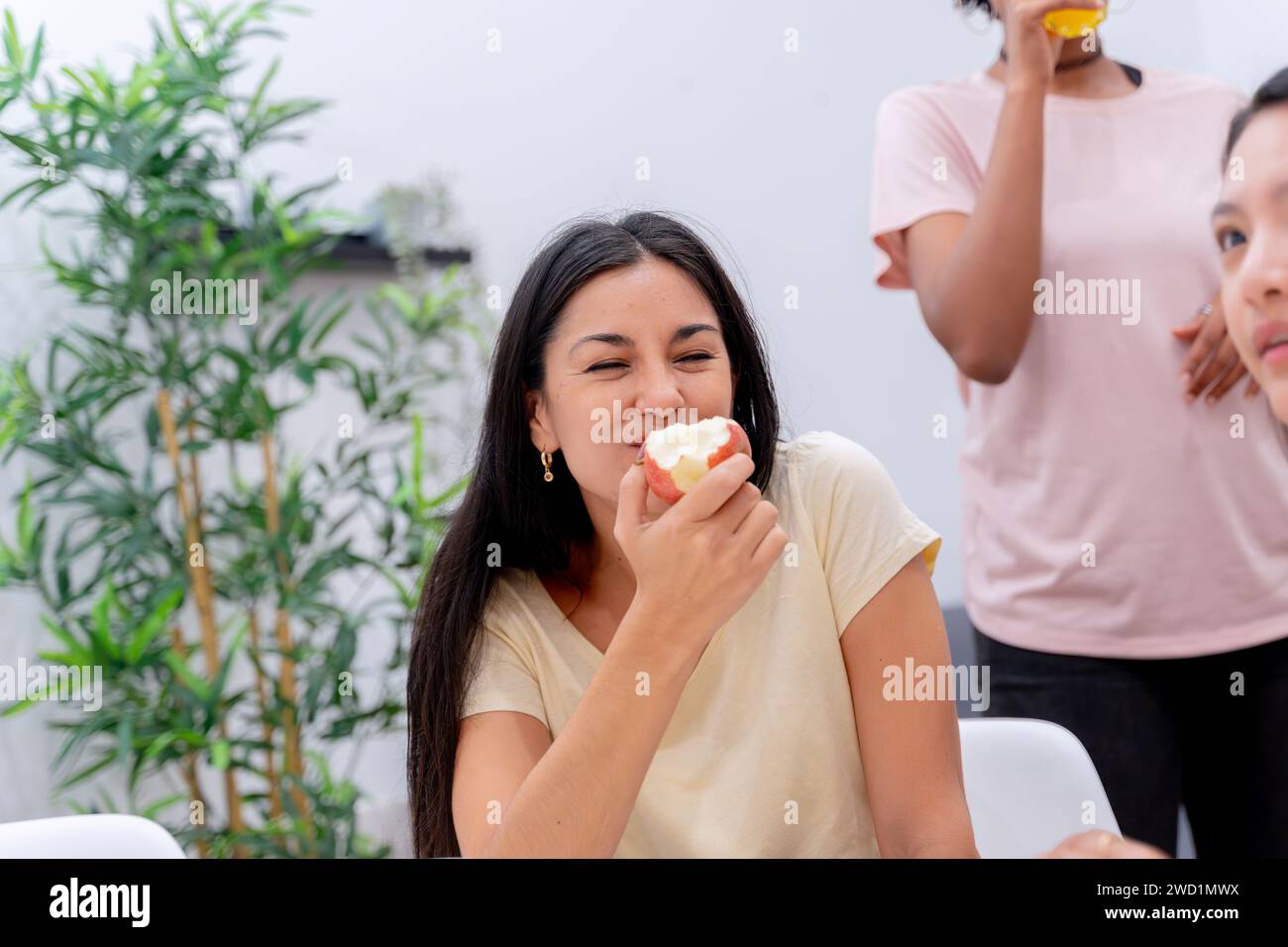 A young woman winks playfully while biting into a crisp apple at a ...