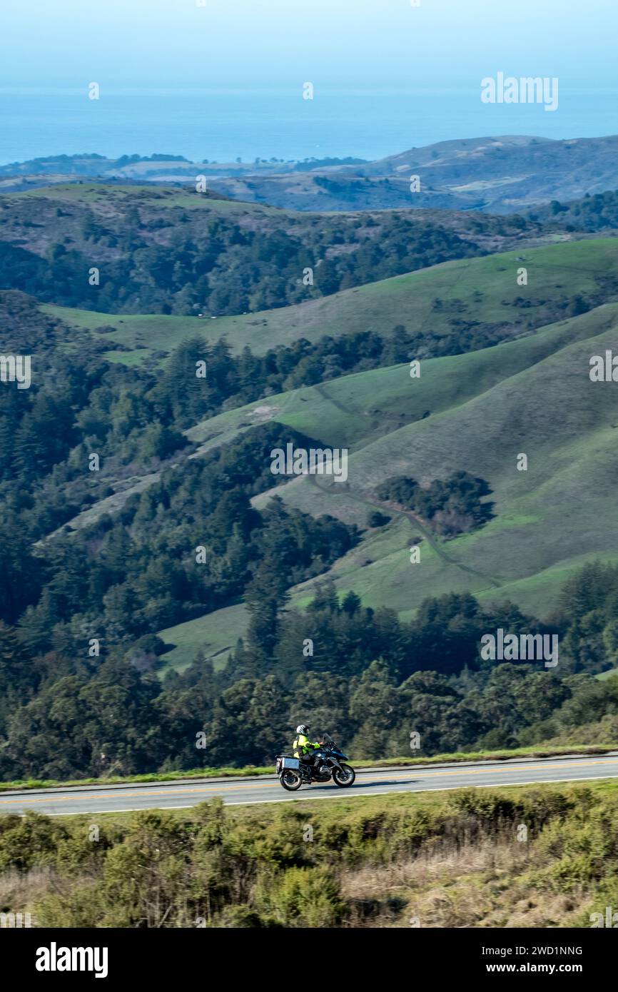A lone motorcycle riding along a mountain ridge with green hills in the ...