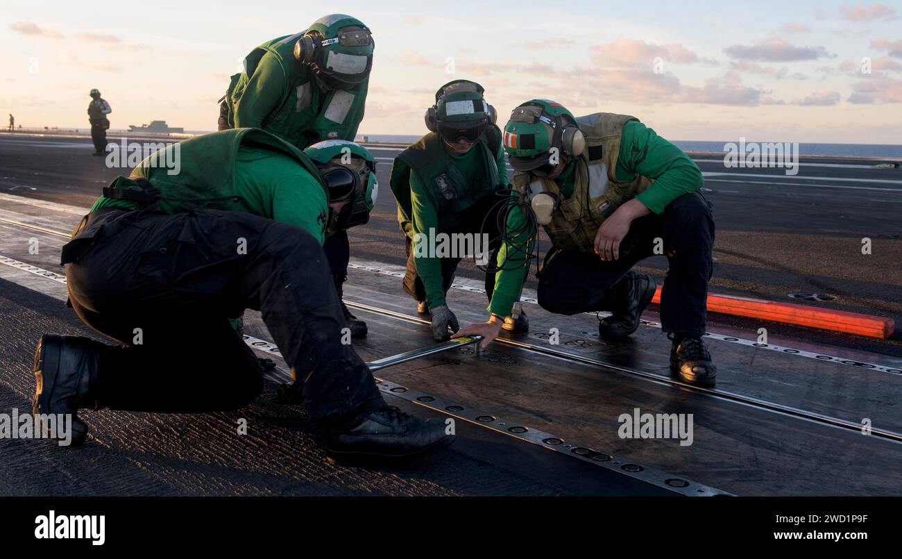 Sailors tighten screws on a catapult track prior to launching an ...