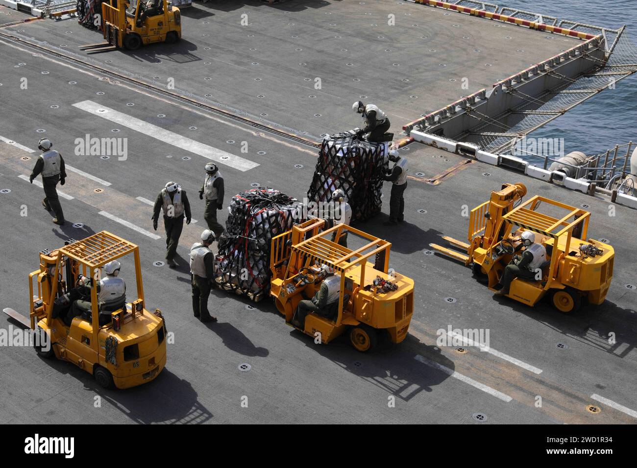 U.S. Marines unload cargo on the flight deck of the amphibious assault ...