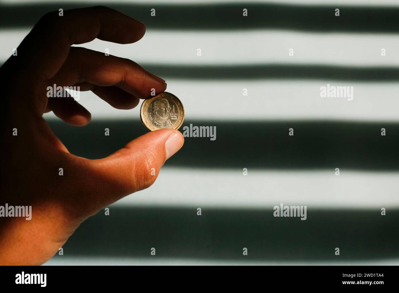 Close up hand holding one euro coin with light and shadow pattern as ...