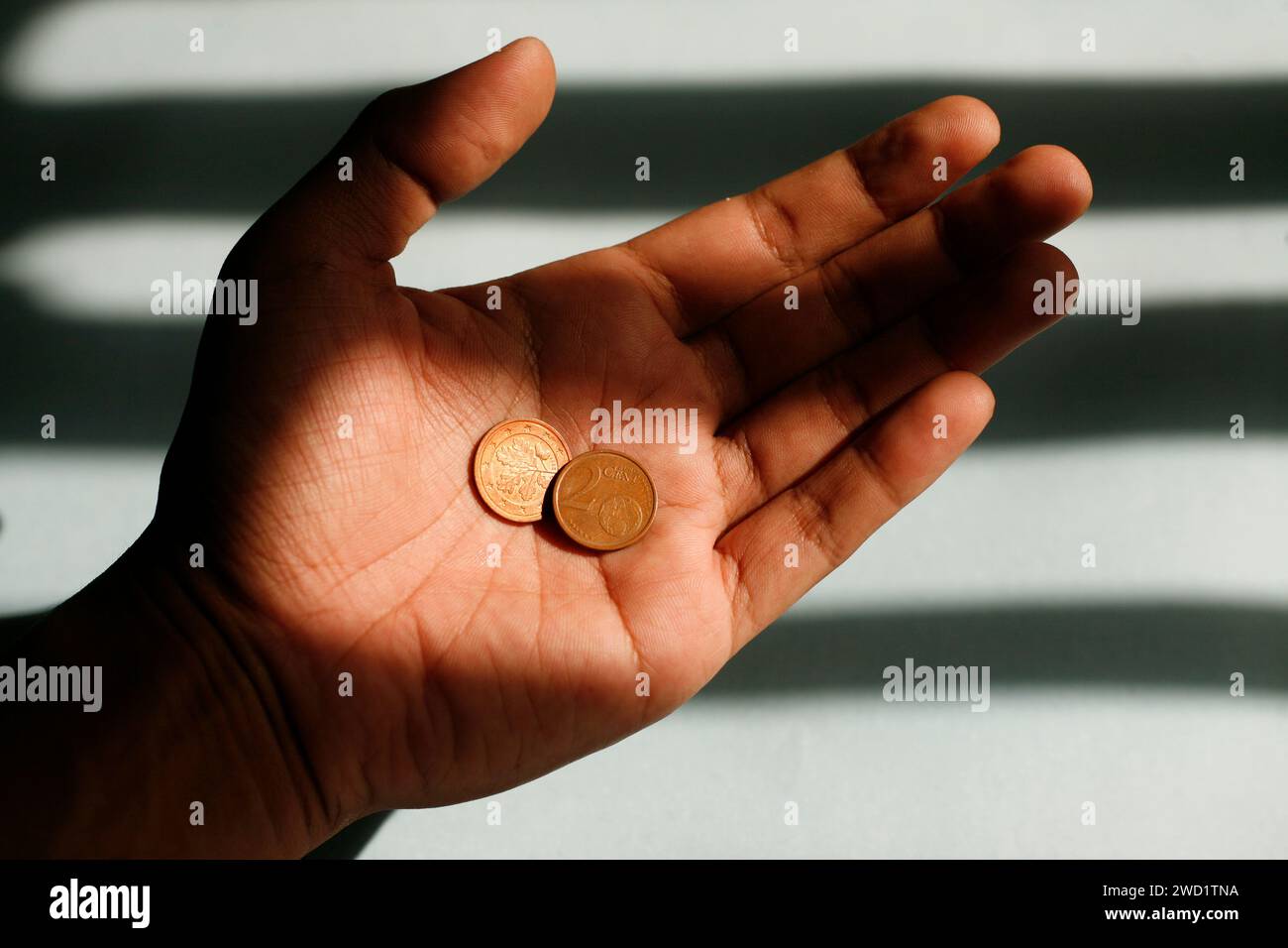 Close up hand holding 2 cent coins euro with light and shadow pattern ...