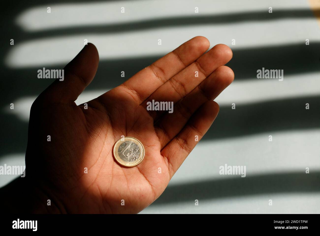 Close up hand holding one euro coin with light and shadow pattern as ...