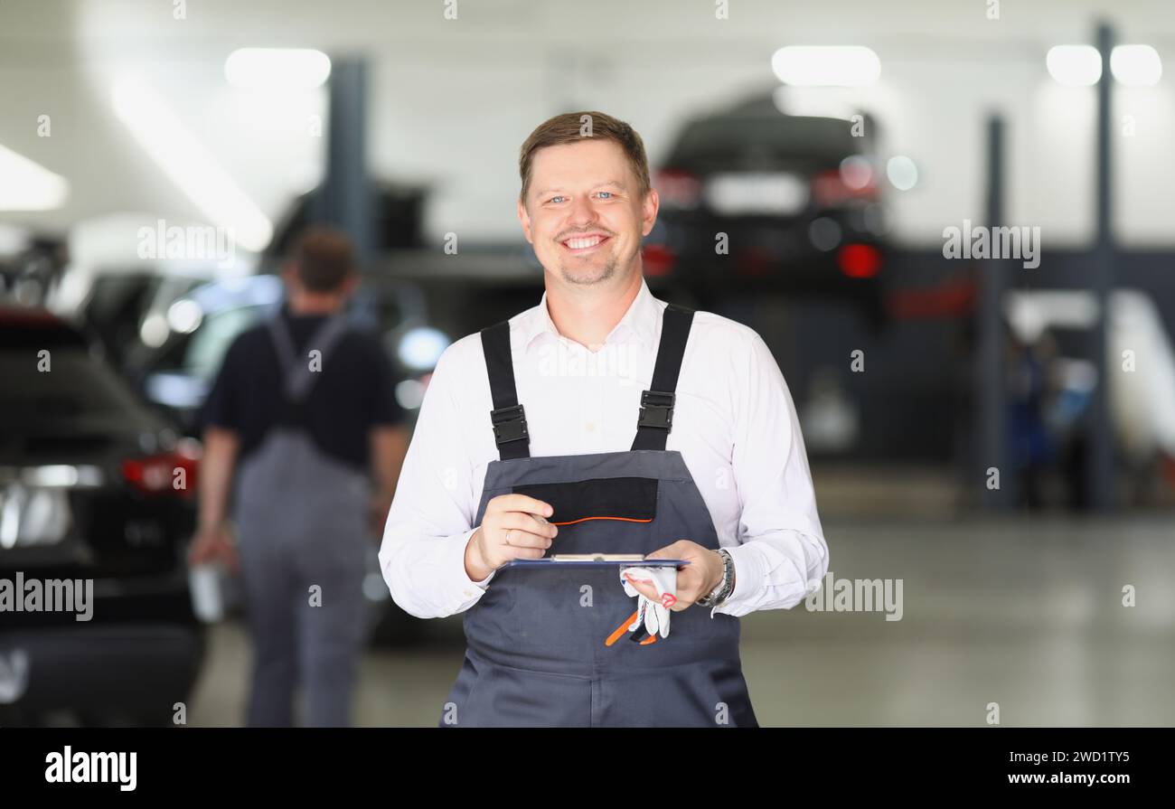 Smiling maintenance center worker in uniform, man fill in papers on car ...