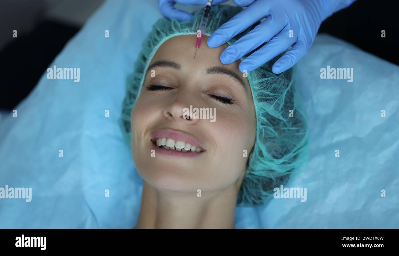 Smiling lady gets injection of botox in her forehead, cosmetologist ...