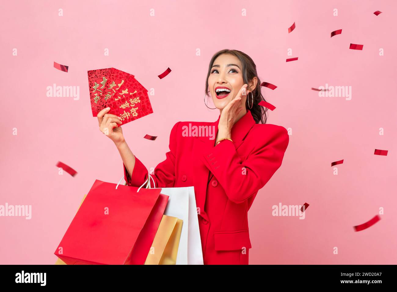 Surprised beautiful Asian woman in red jacket carrying shopping bags ...