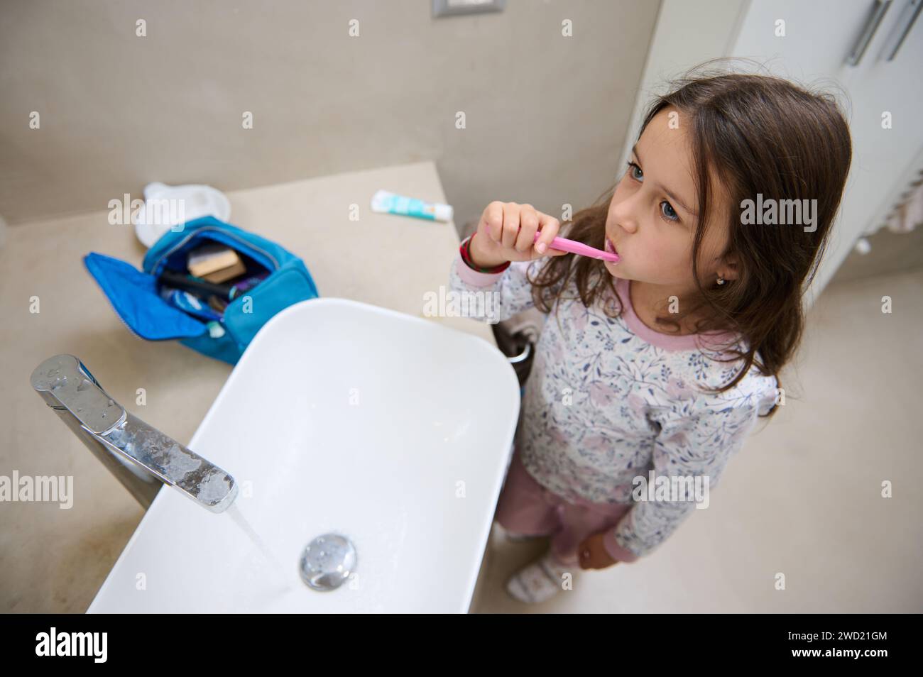 View from above of a little child girl brushing teeth, standing at ...