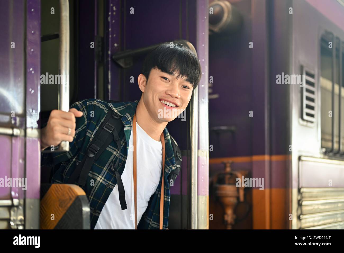 Happy male tourist with backpack getting off the train and peeking out ...
