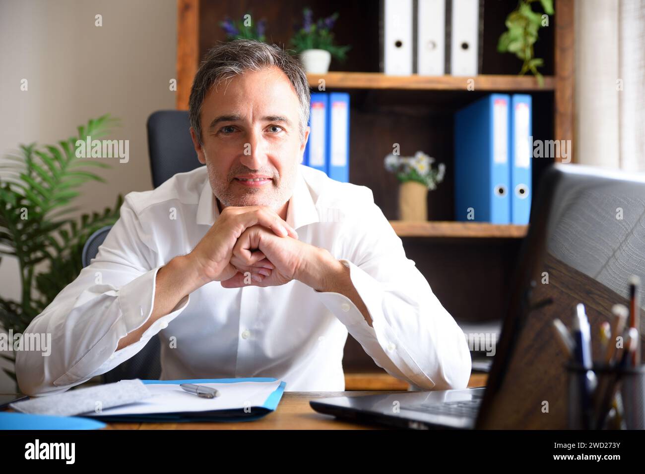 Man in white shirt at work smiling leaning on an office table looking ...