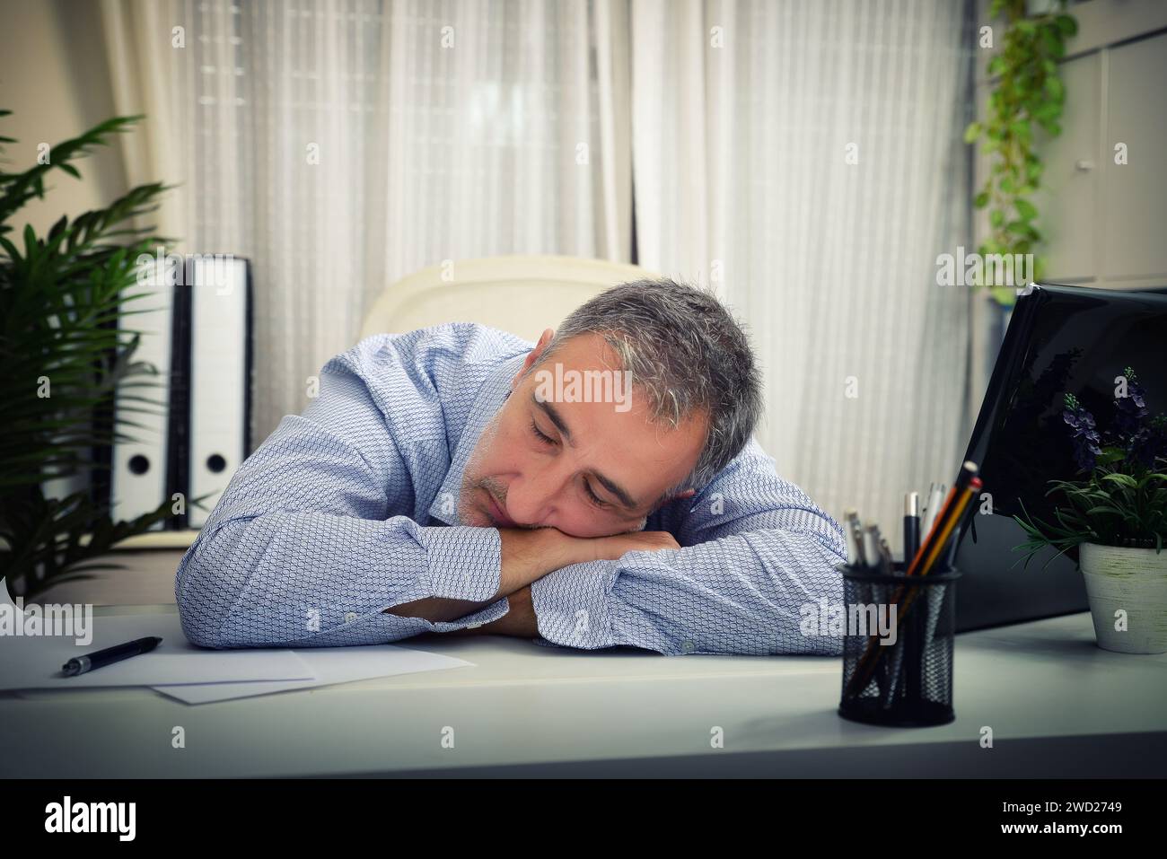Detail of a man sleeping on an office table with a laptop and pen in an ...