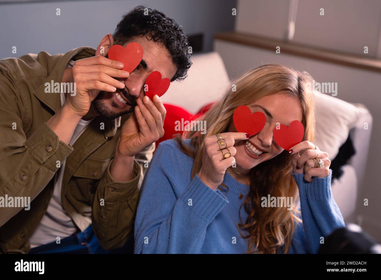 Close-up photo of happy couple in love hiding eyes behind paper hearts ...
