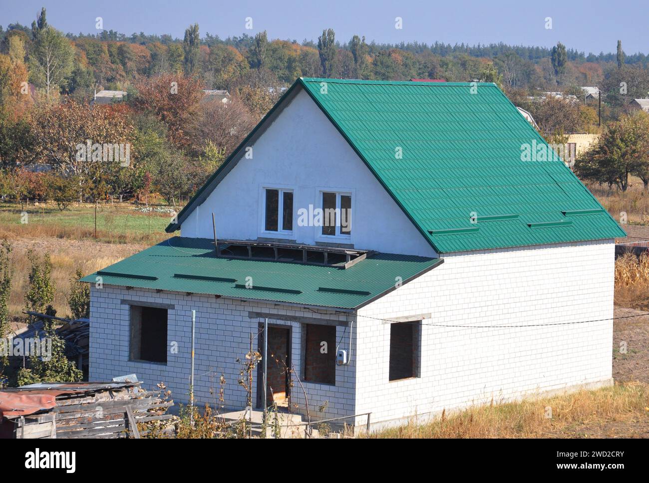 An exterior view of incomplete white brick house with attic green metal ...