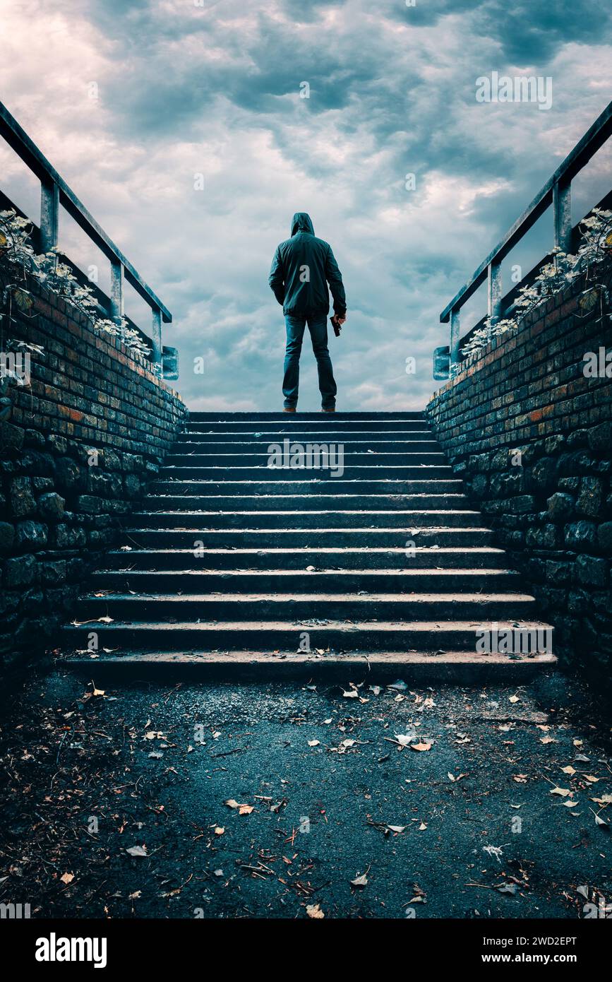 Hooded man with a hand gun standing at the top of stone steps Stock ...
