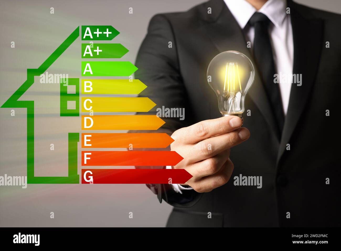 Energy efficiency rating and man holding glowing light bulb on grey ...