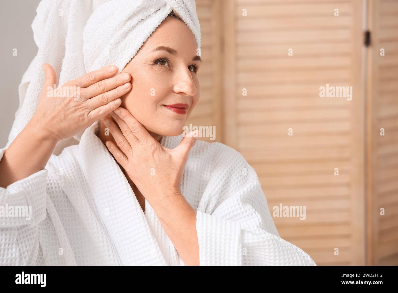 Mature woman doing face building exercise after shower in bathroom ...